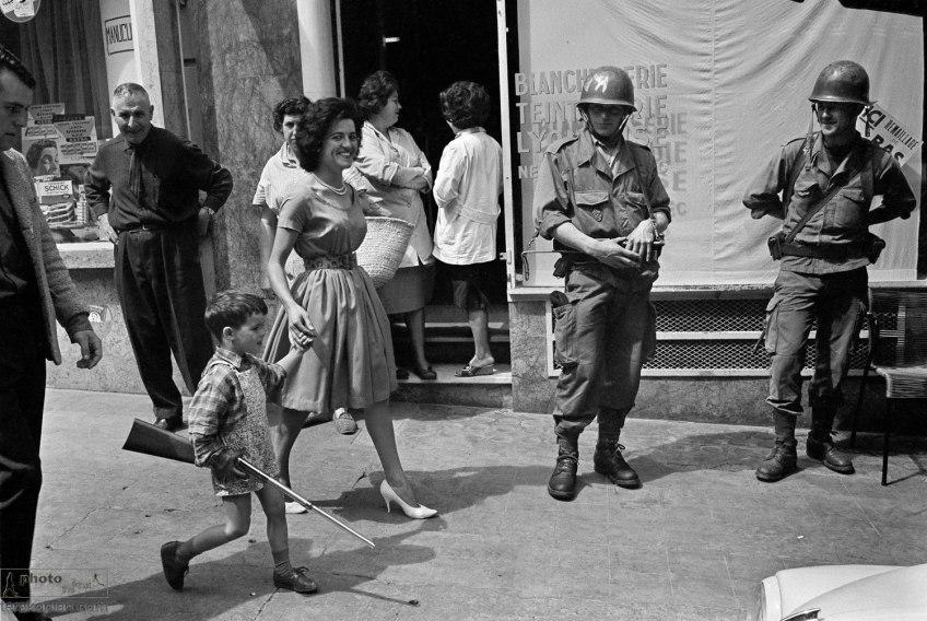 A boy walking with his mother past French soldiers in battle gear