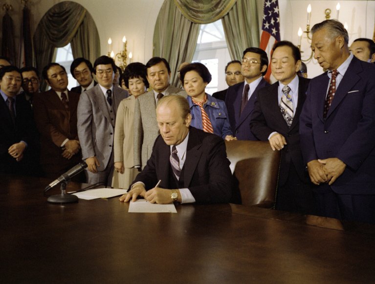 Ford signs papers to rescind the order while Asian Americans watch.